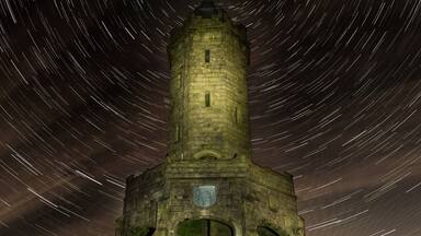 Uma torre de pedra com rastros de estrelas no céu noturno.