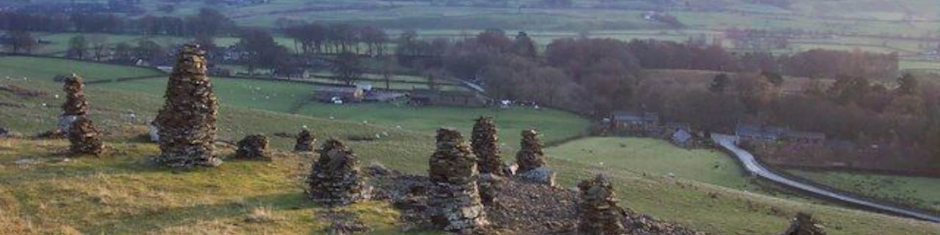 Paisagem rural com colinas onduladas, montes de pedra espalhados e uma estrada sinuosa.