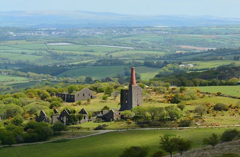 Paisagem rural com uma igreja de pedra imponente, alguns edifícios menores e campos verdes ondulantes.