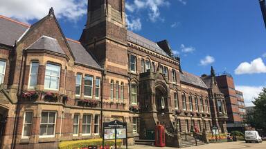 Um edifício histórico com uma torre do relógio, uma cabine telefônica vermelha e uma placa de boas-vindas a St. Helens.
