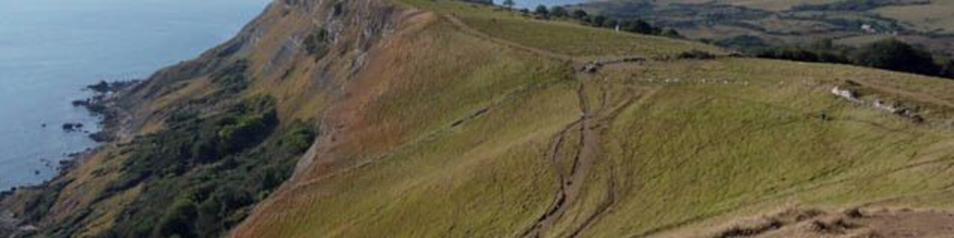 Paisagem costeira com colinas gramadas e falésias a debruçar sobre o mar.