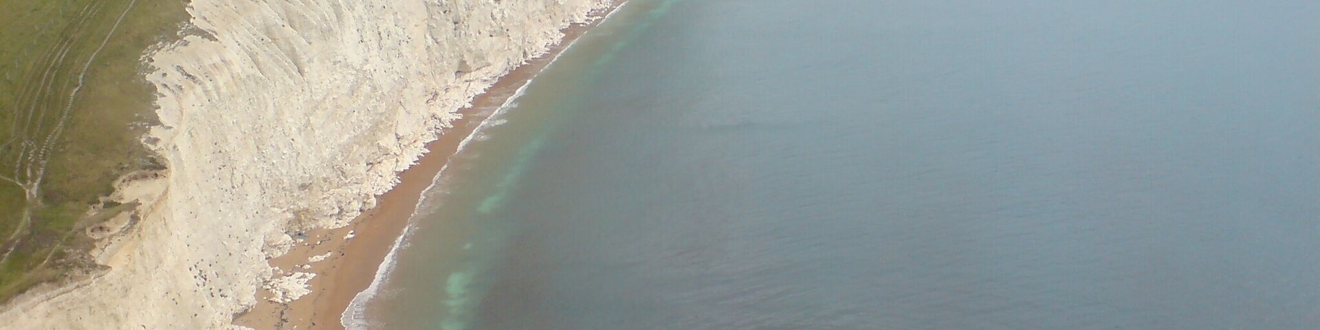 Paisagem costeira com falésias, uma praia arenosa e uma grande formação rochosa no mar.