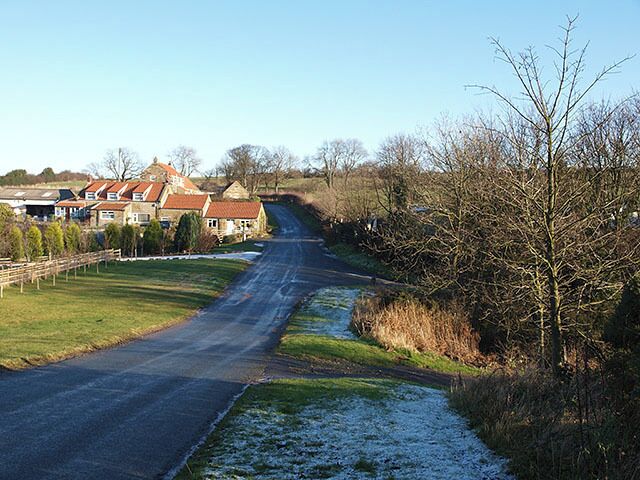Uma estrada rural com casas de um lado e um rio do outro.
