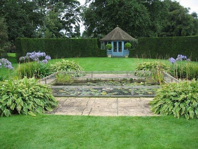 Um jardim com lago, um gazebo e sebes bem aparadas.