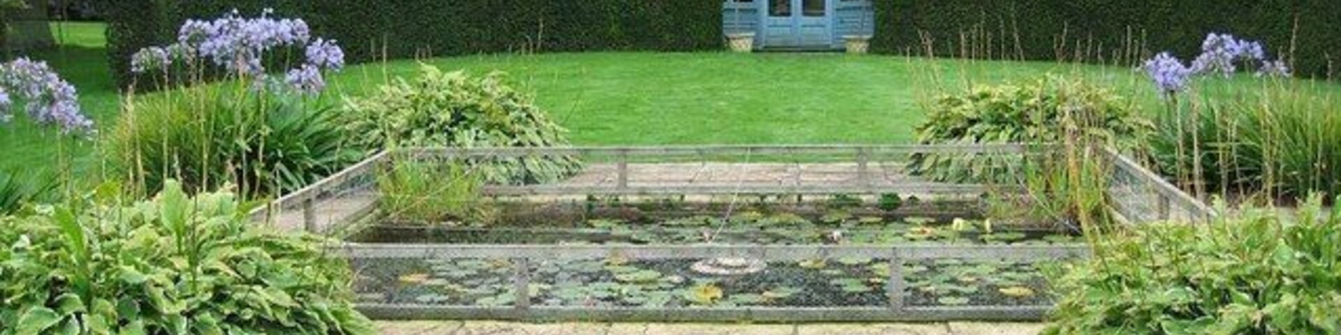 Um jardim com lago, um gazebo e sebes bem aparadas.