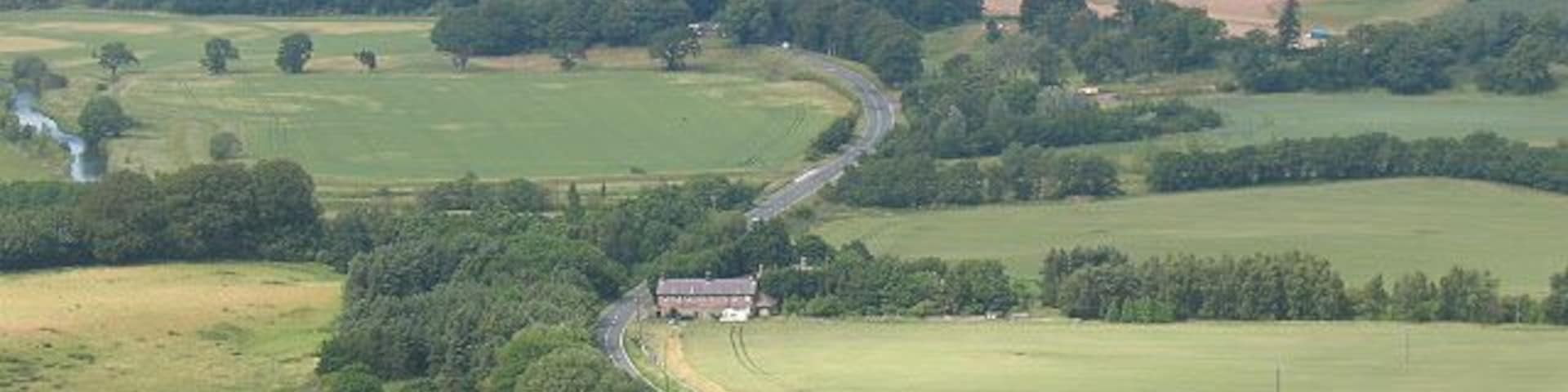 View over Akeld from the south. The large complex of buildings in the foreground of the photo is the country club 1248370, which dominatees the settlement. A little further along the main road is the old station 309714.