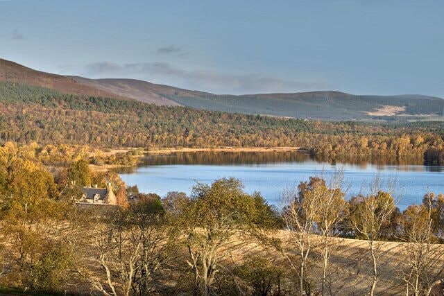 Um lago rodeado por árvores e colinas com tons de outono.