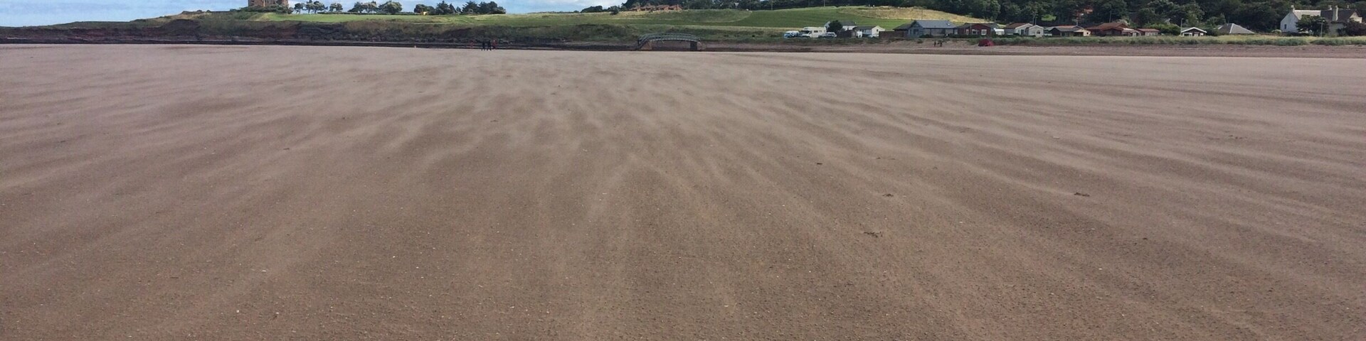 Uma extensa praia de areia com céu claro e edifícios ao longe.