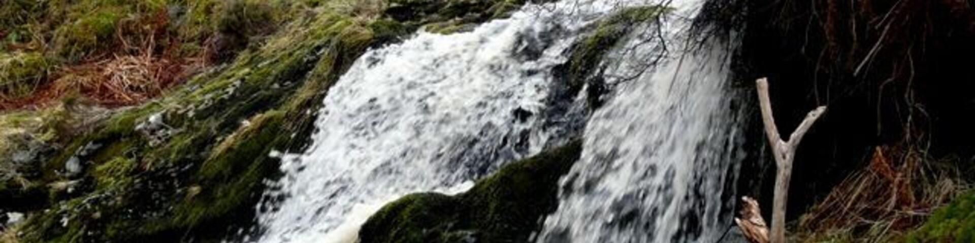 Uma cascata em cascata, rodeada por rochas cobertas de musgo e vegetação escassa.