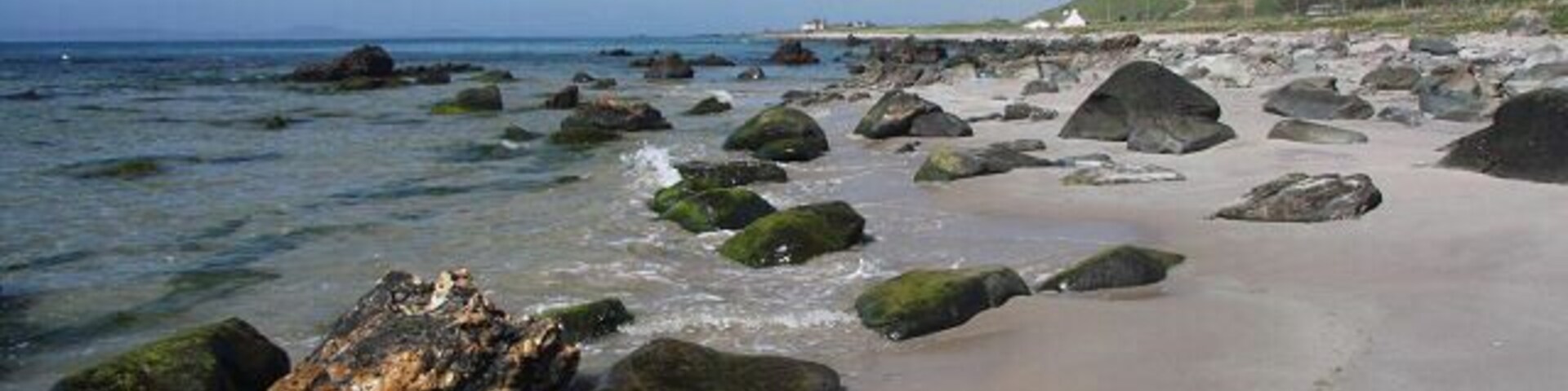 Uma praia rochosa com águas cristalinas e uma colina ao longe.