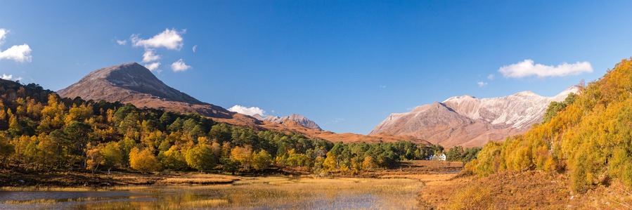 Paisagem montanhosa com árvores de cores outonais, um lago e uma pequena casa no vale.