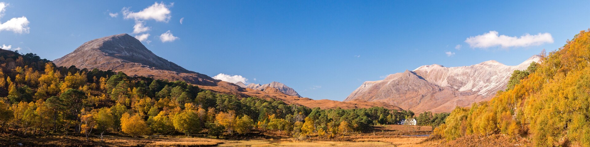 Paisagem montanhosa com árvores de cores outonais, um lago e uma pequena casa no vale.
