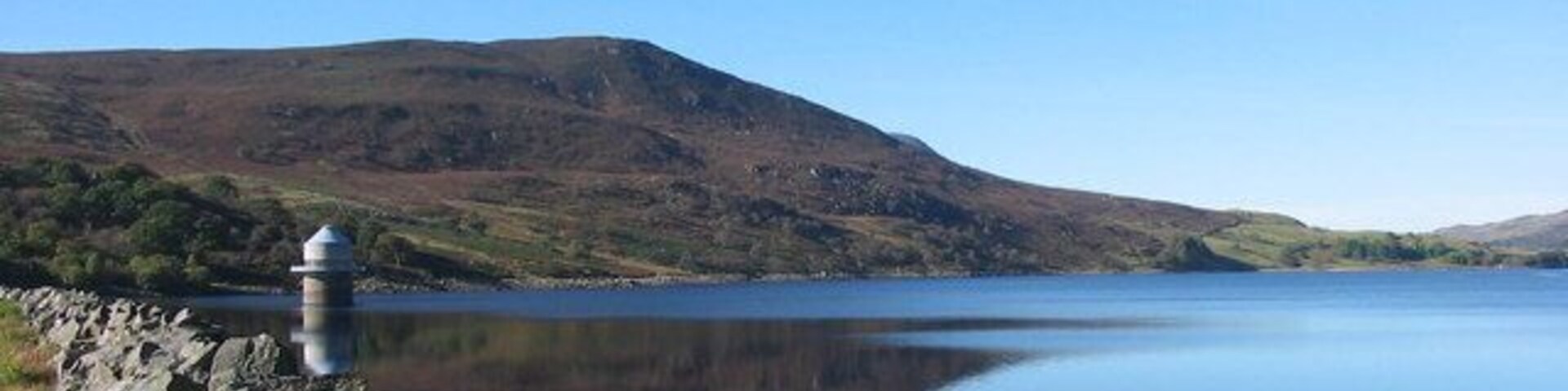 Um lago tranquilo com margens rochosas e uma colina ao fundo.