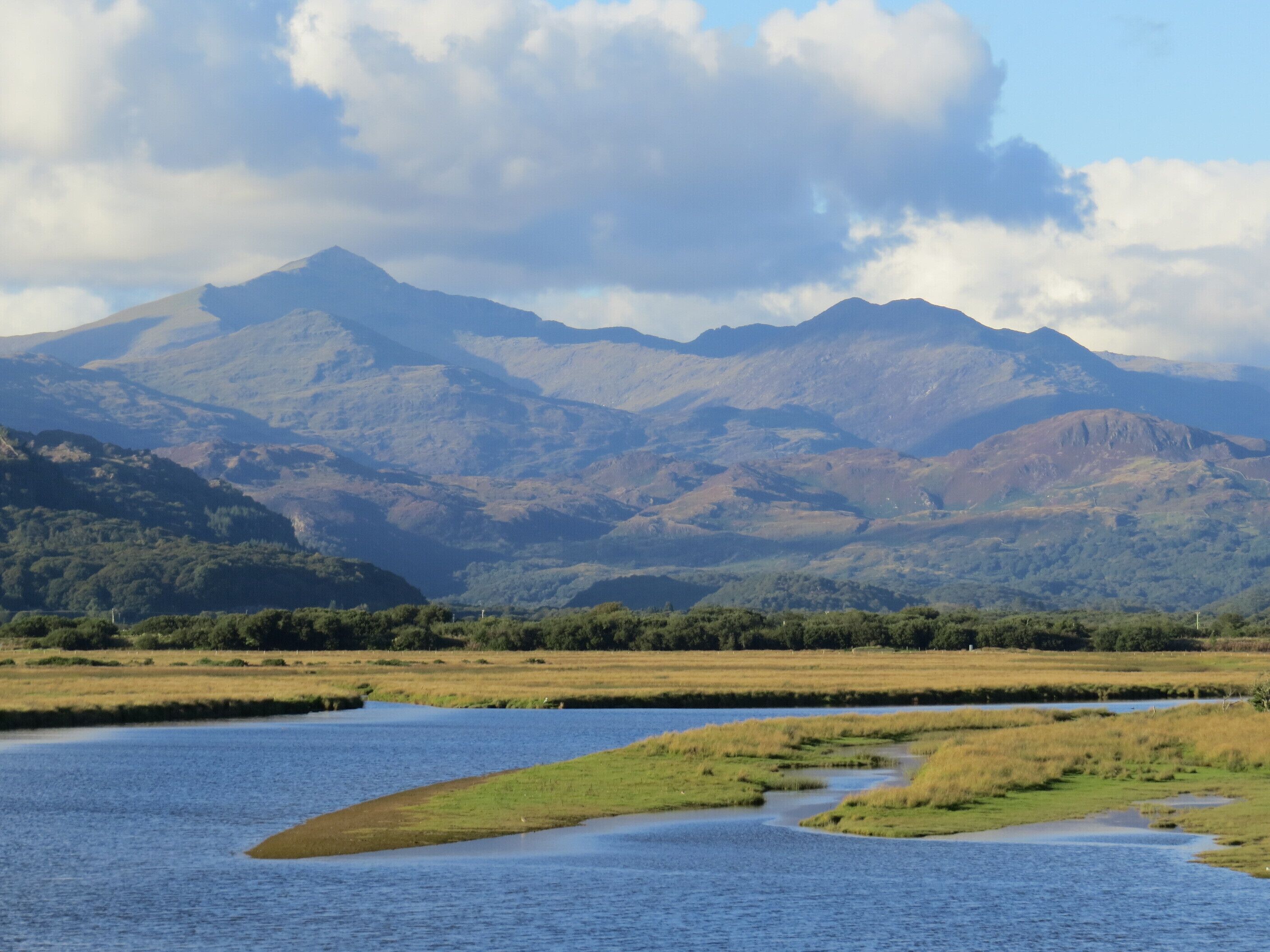 Um rio serpenteando por um vale, com montanhas ao fundo.