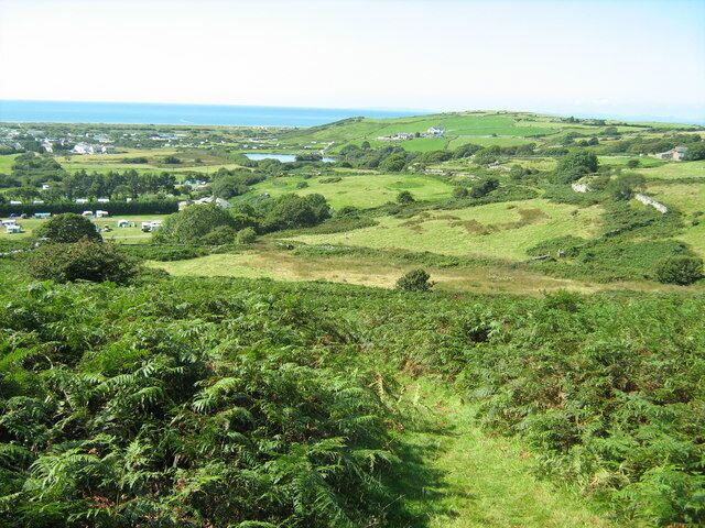Paisagem costeira com colinas ondulantes, campos verdes e casas salpicadas.