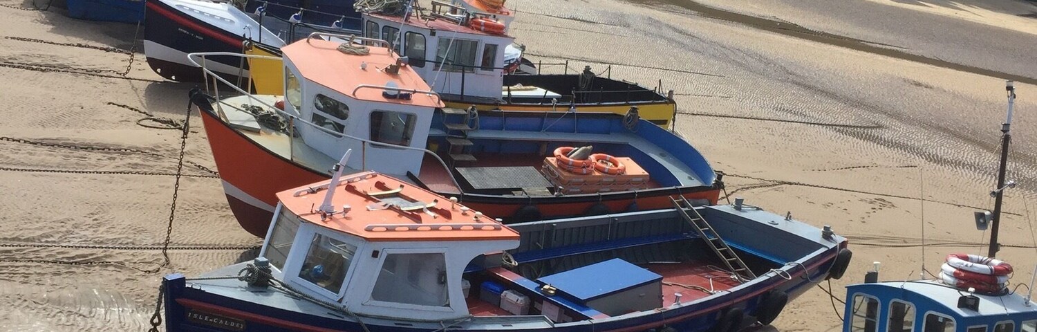 A lone sailor takes the opportunity to clean his boat during low tide on beautiful Tenby harbour beach. The pretty houses in the background are characteristic of this old Welsh town