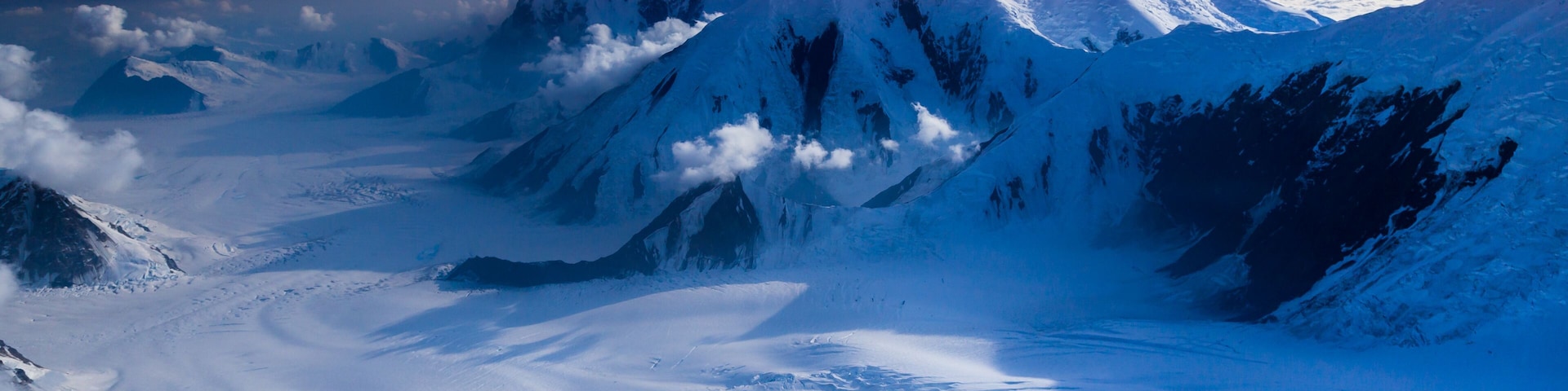 Cordilheira nevada com um pico imponente e um vale abaixo.