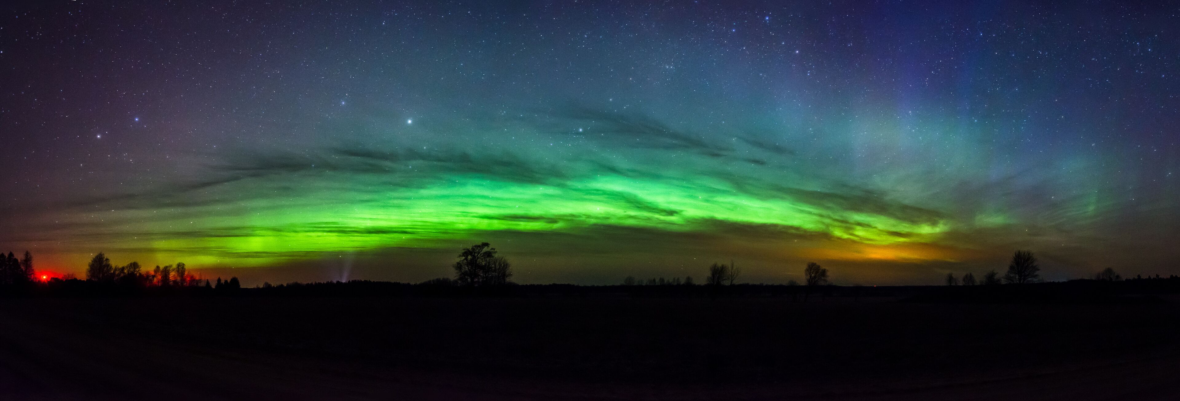 Céu noturno com a aurora boreal sobre uma paisagem florestal.