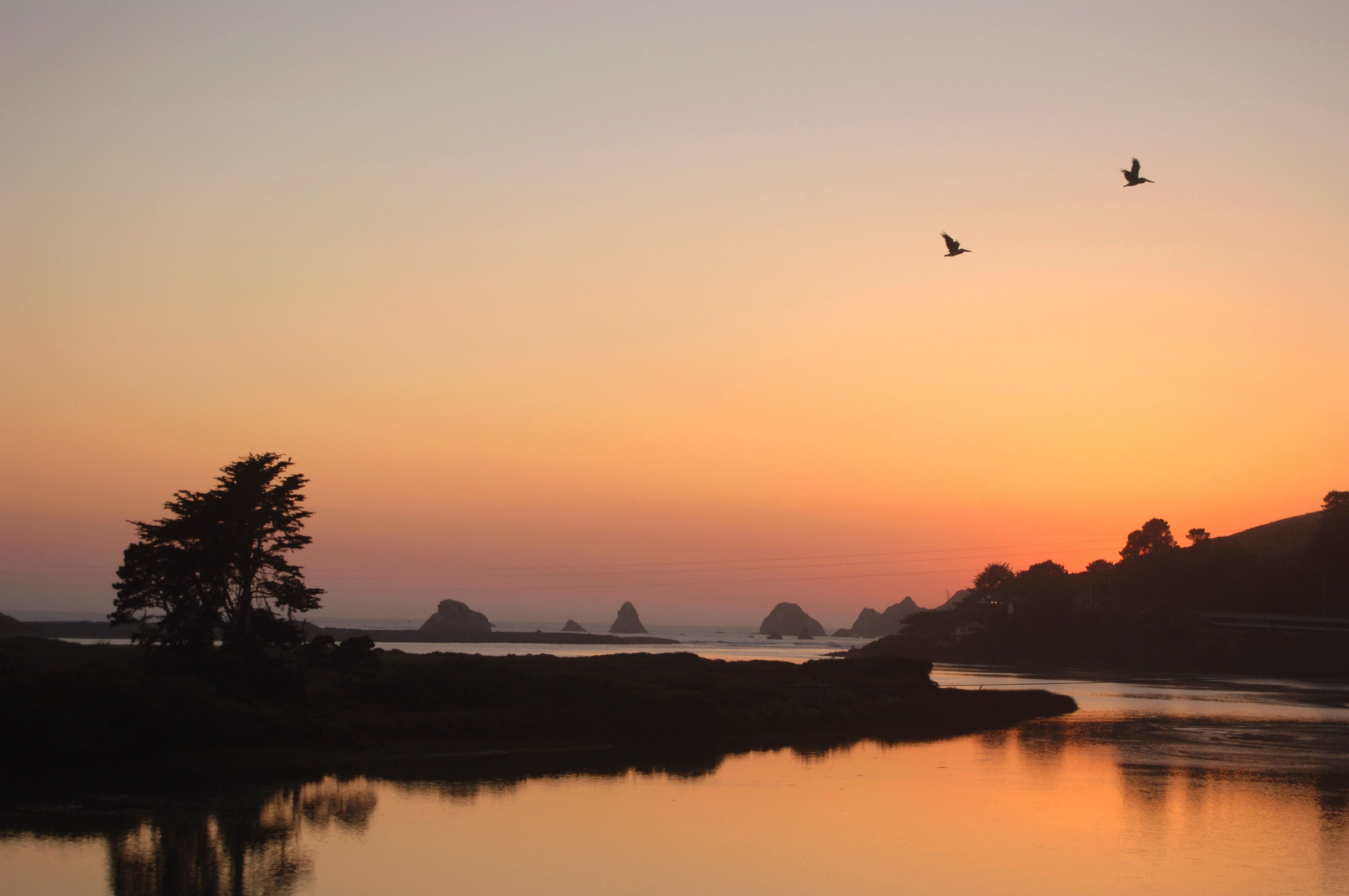 Um pôr do sol sobre um rio calmo, com silhuetas de árvores e formações terrestres ao longe.