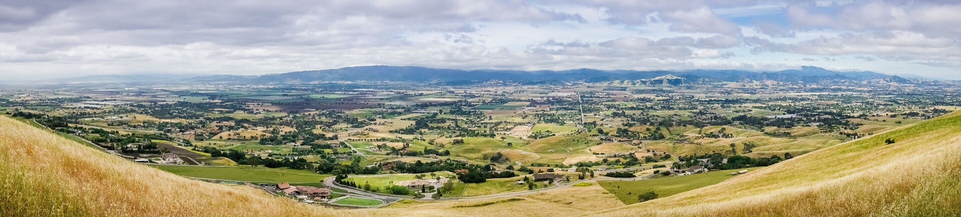 Vista panorâmica de uma paisagem rural com colinas ondulantes, campos e montanhas ao longe.
