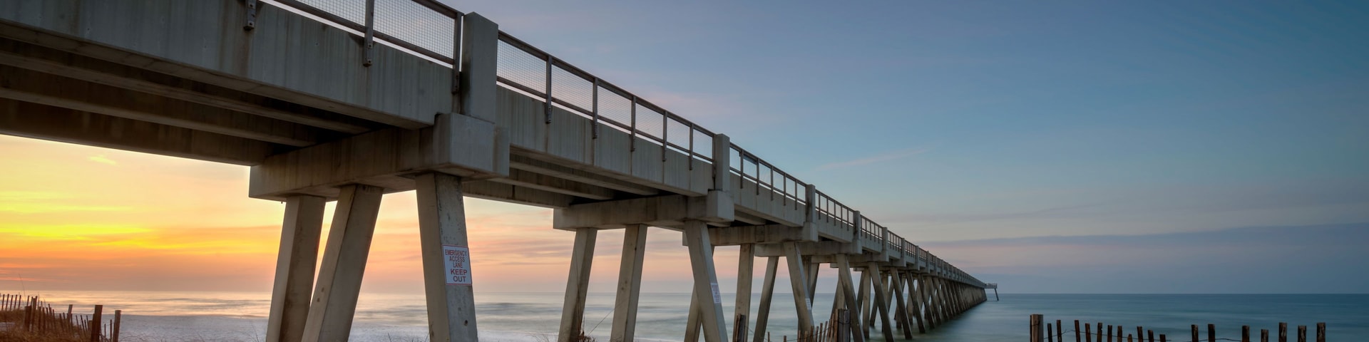 Um cais se estende sobre a praia ao pôr do sol.