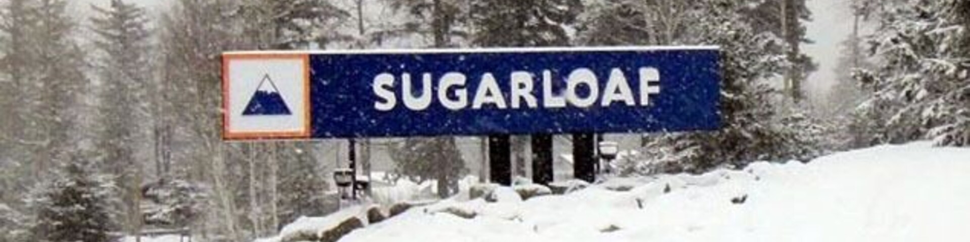 Montanha coberta de neve com uma placa indicando "SUGARLOAF".