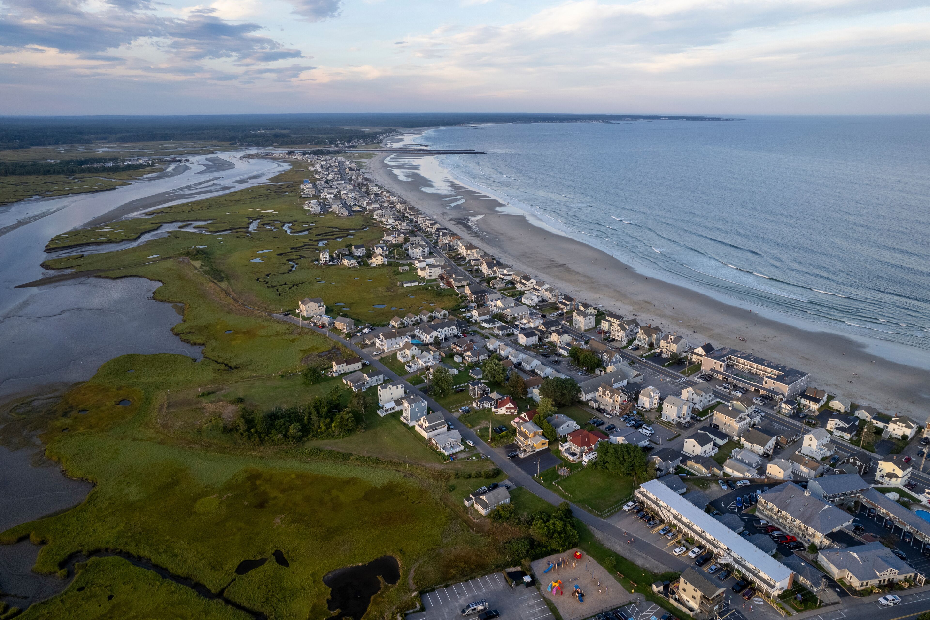 Vista aérea de uma cidade costeira com praia, áreas pantanosas e edifícios residenciais.