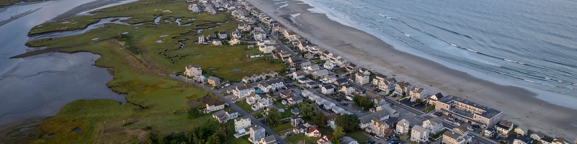 Vista aérea de uma cidade costeira com praia, áreas pantanosas e edifícios residenciais.
