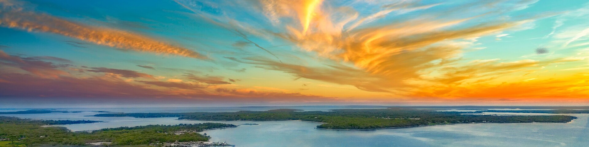 Paisagem costeira com pôr do sol, um porto de iates e uma área residencial.