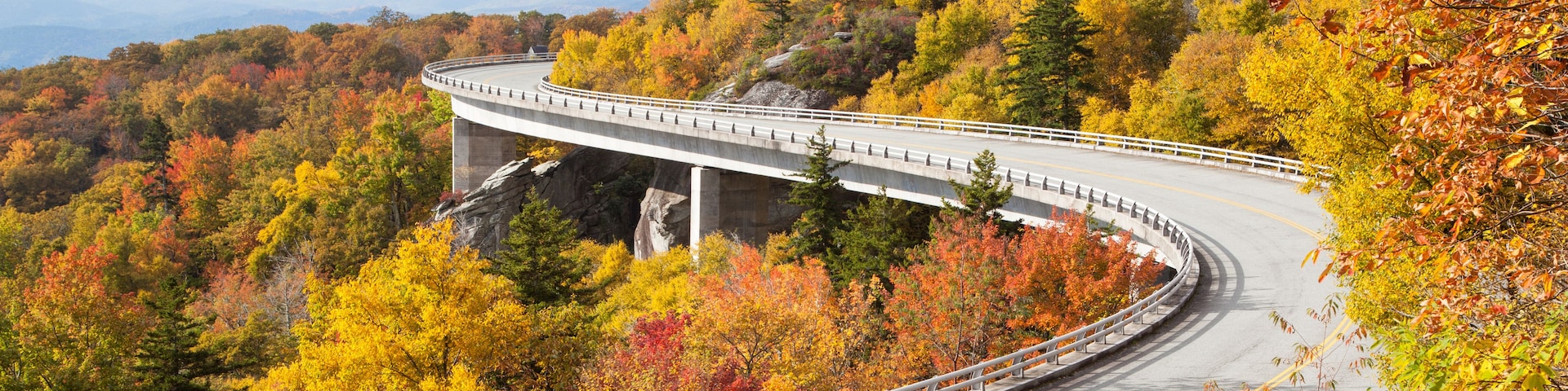 Estrada sinuosa com uma ponte sobre uma área montanhosa arborizada.