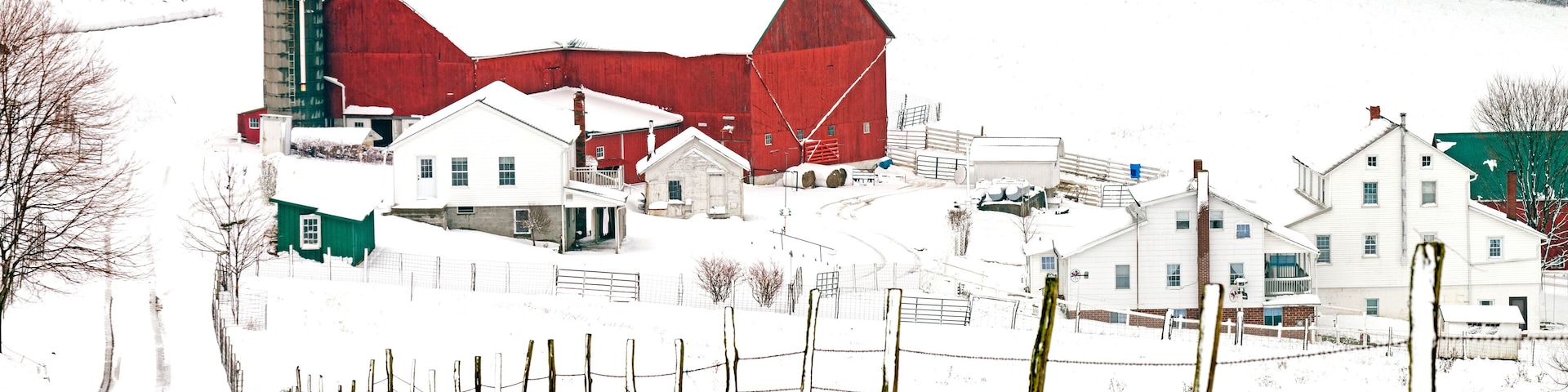 Uma quinta coberta de neve, com um celeiro vermelho, um silo e várias casas brancas.