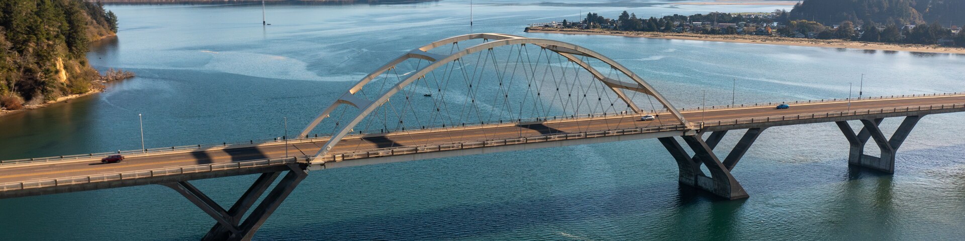 Uma grande ponte suspensa atravessa um rio largo, com paisagem arborizada e montanhas ao fundo.