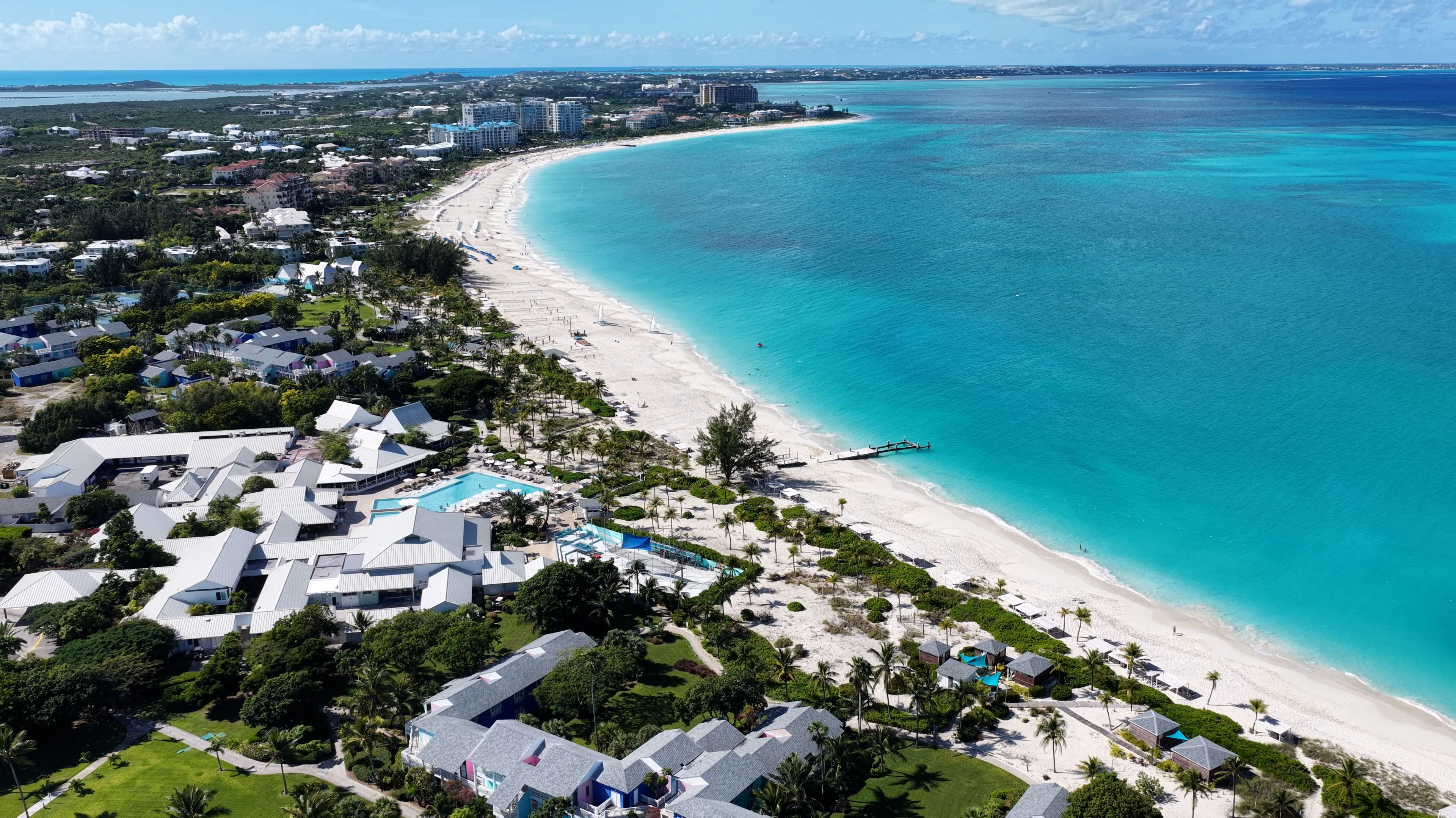 Uma área costeira com resort, praia, águas azul-claras e edifícios residenciais e de resort.