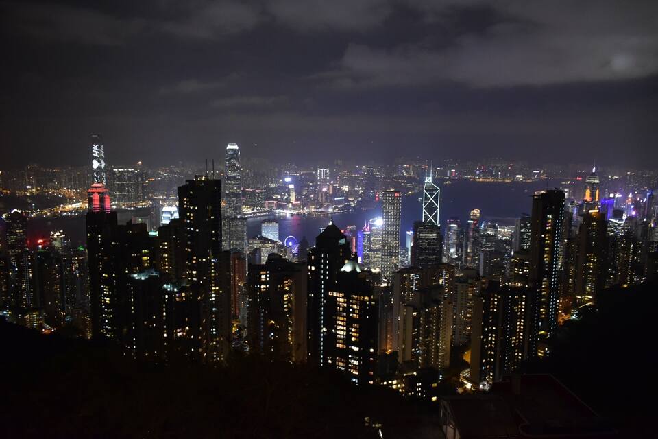 Paisagem urbana noturna com arranha-céus iluminados e uma torre destacada com iluminação vermelha.