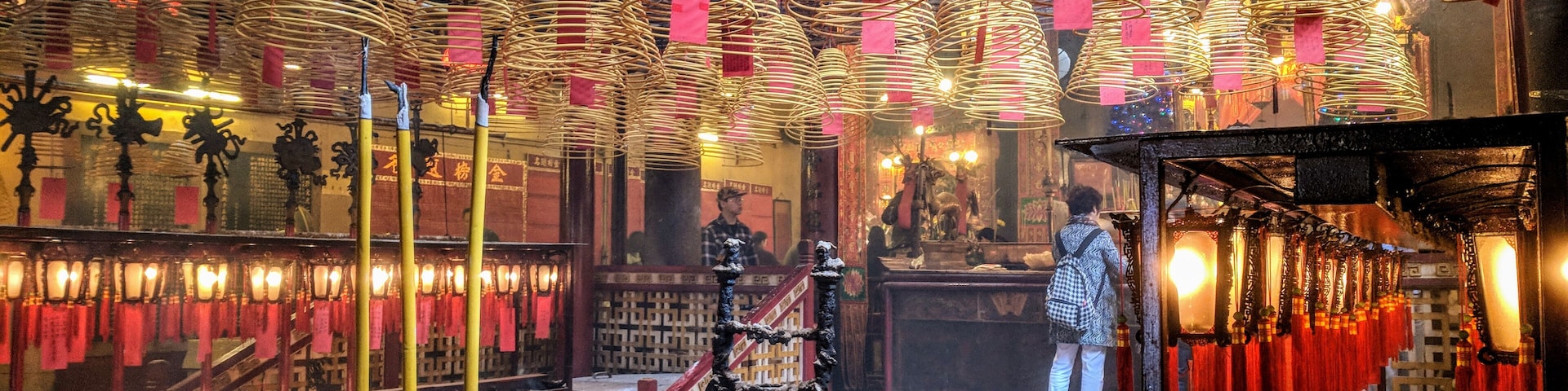 Interior de templo com queimadores de incenso pendurados, uma estátua de leão e uma escadaria.