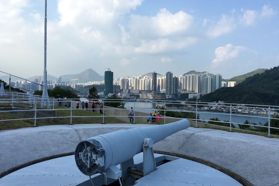 Um telescópio numa plataforma com vista para uma paisagem urbana, com um rio e montanhas ao fundo.