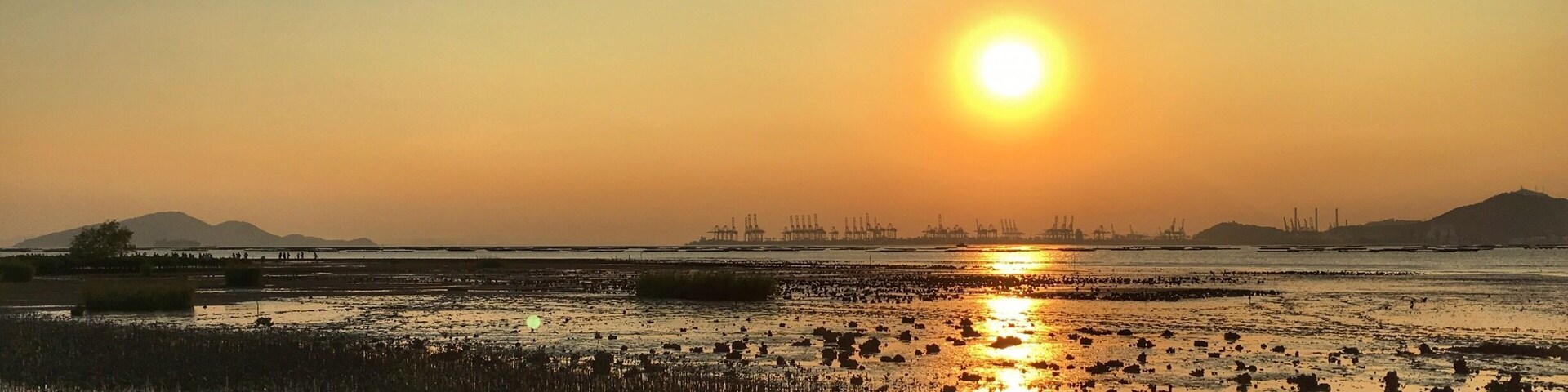 Um pôr do sol sobre uma área costeira com estruturas industriais ao fundo.