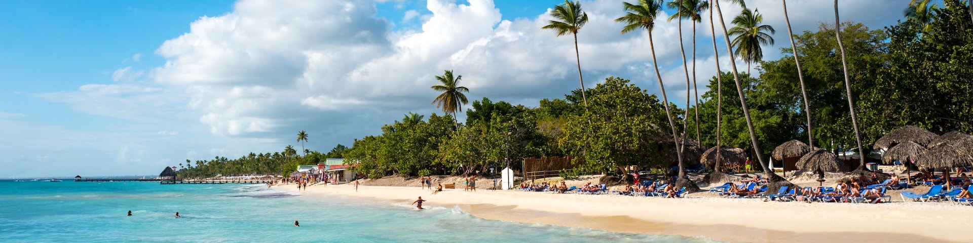 Uma praia tropical com águas turquesa cristalinas, palmeiras e um píer ao longe.