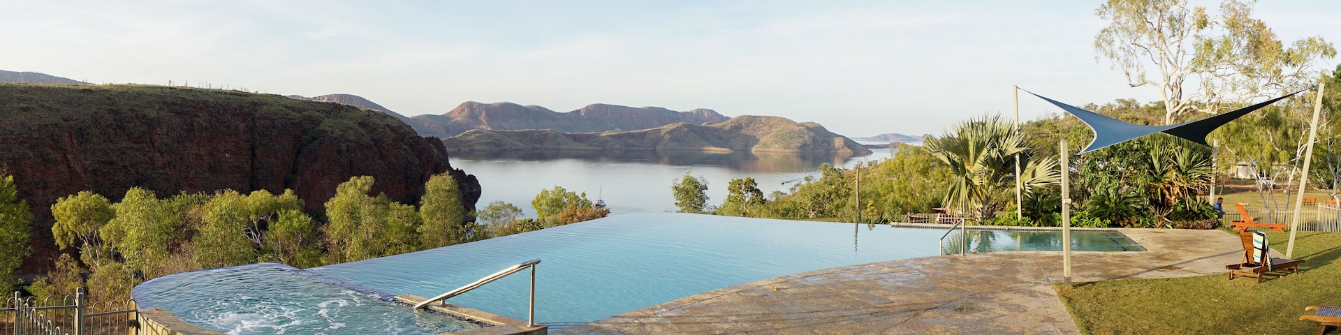 Ofurô e piscina infinita com vista para um lago, com montanhas ao fundo.