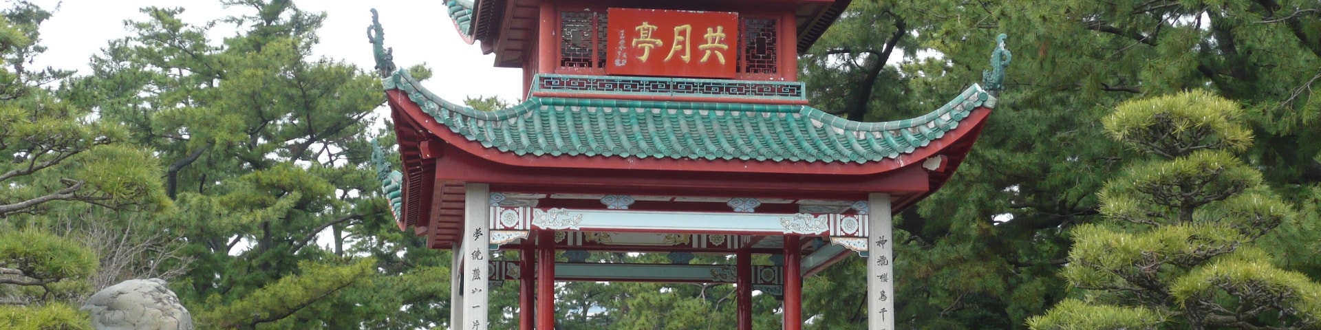 Um pavilhão tradicional chinês com cores verde e vermelha, rodeado por árvores e pedras.