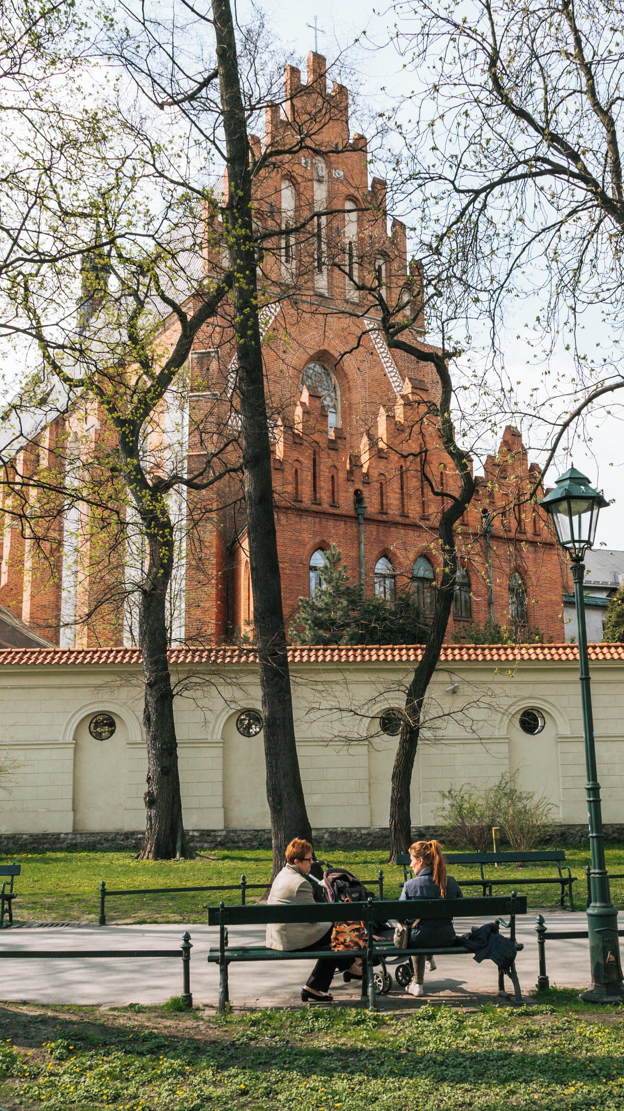 Views of Holy Trinity Church in Kraków's city center with visitors enjoying a peaceful afternoon in a nearby park during springtime