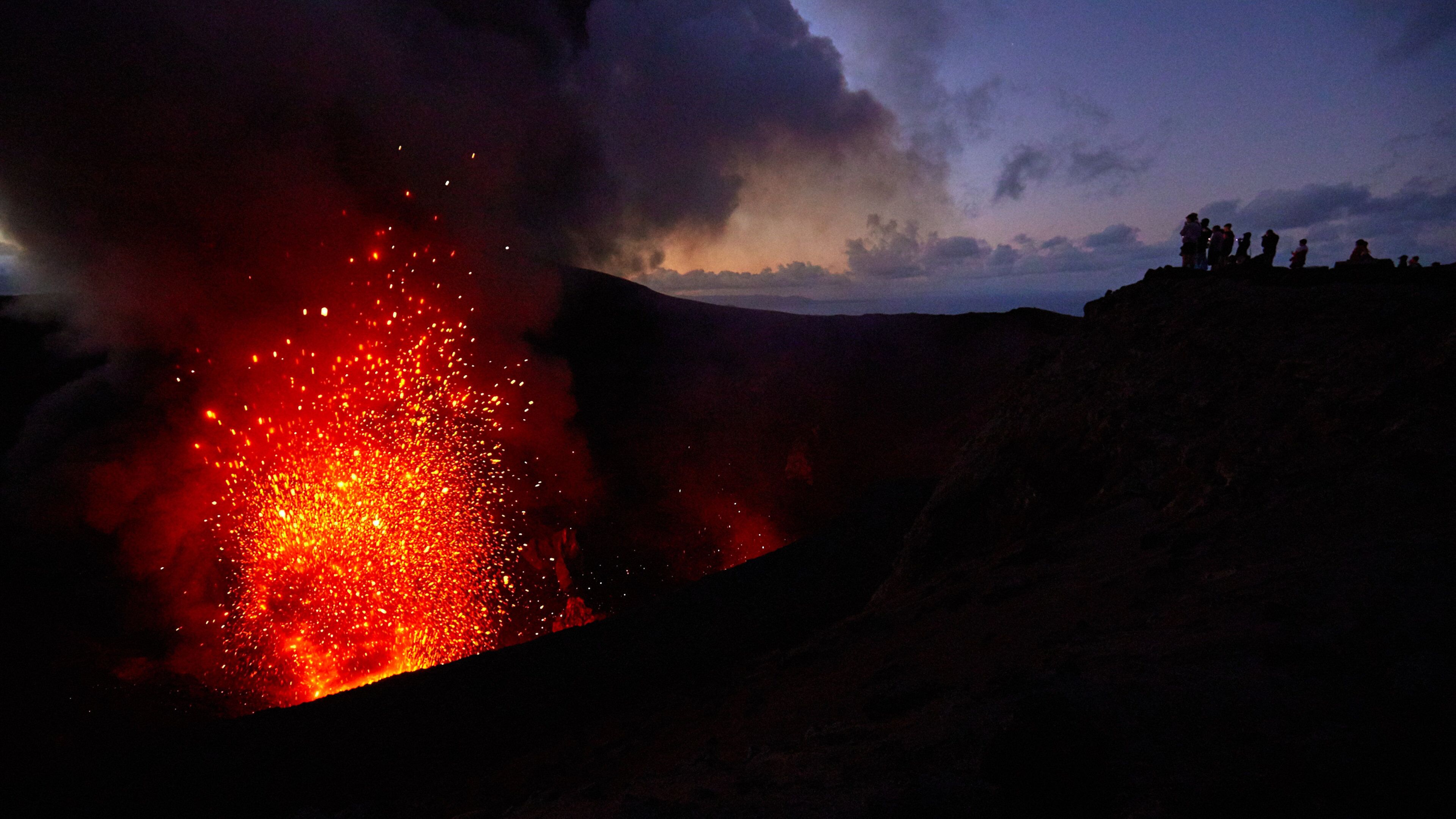 Uma erupção vulcânica com lava escorrendo pela encosta de uma montanha.