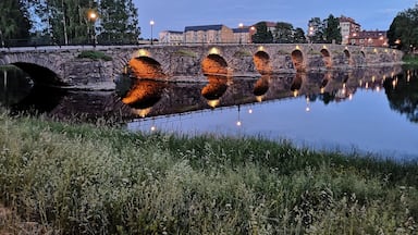 Uma ponte de pedra sobre um rio calmo ao entardecer, com luzes refletindo na água.