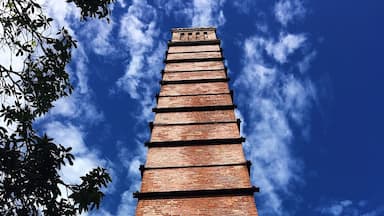 Uma torre de tijolos alta, com um céu azul claro e nuvens ao fundo.