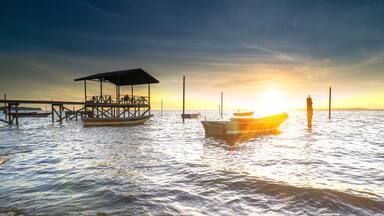 Um cais com área de estar coberta e um barco ancorado ao pôr do sol.