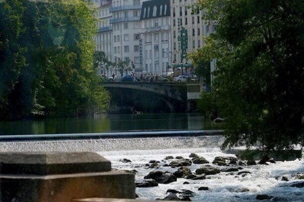 Um rio com pedras, uma ponte e edifícios ao fundo.
