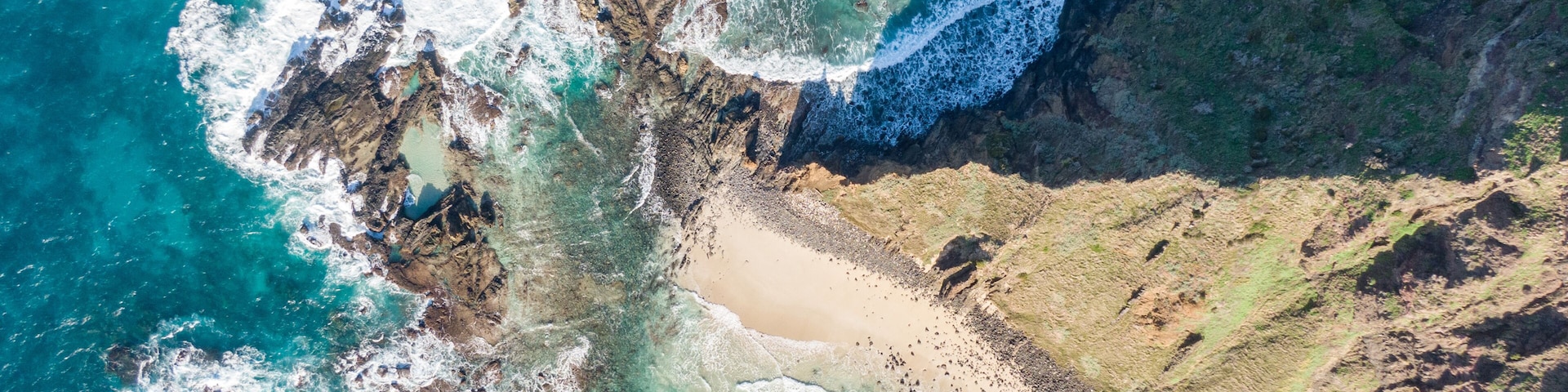 Paisagem costeira com águas turquesa límpidas, falésias rochosas e uma praia arenosa.