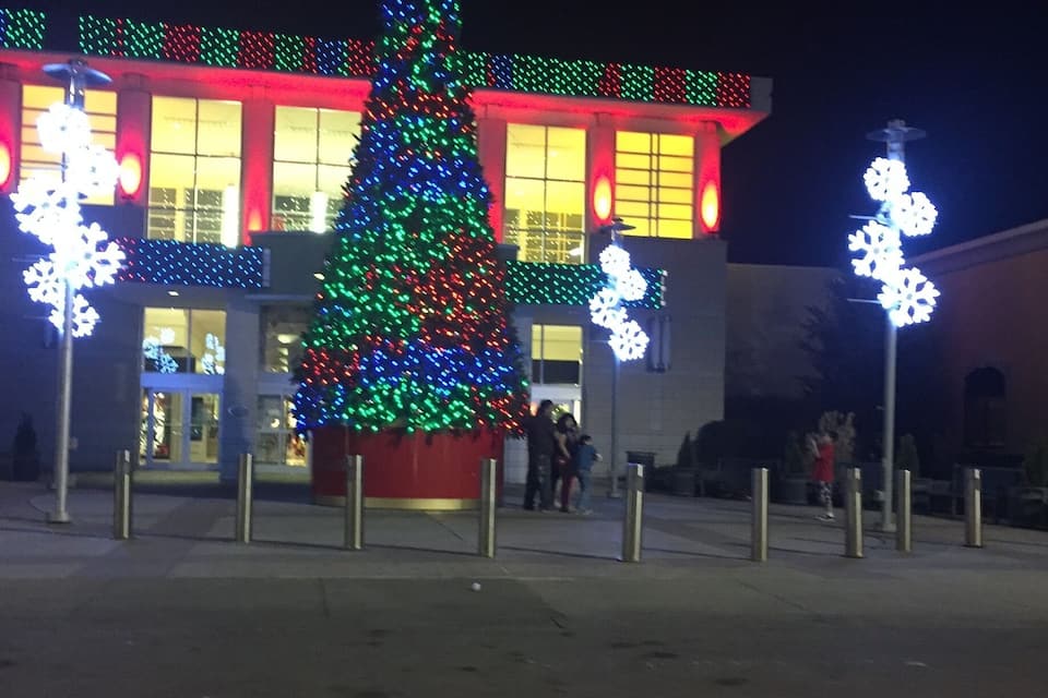 Uma árvore de Natal bem iluminada em frente a um edifício com luzes coloridas.