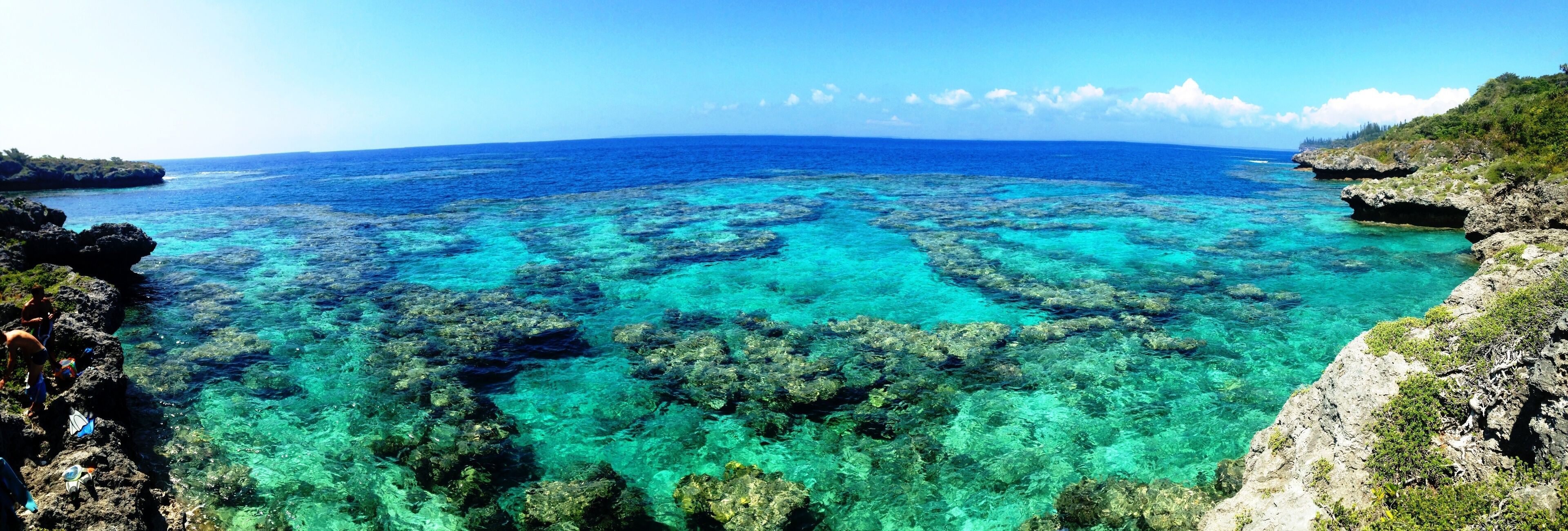 Mar azul cristalina com recifes de coral visíveis e falésias rochosas.