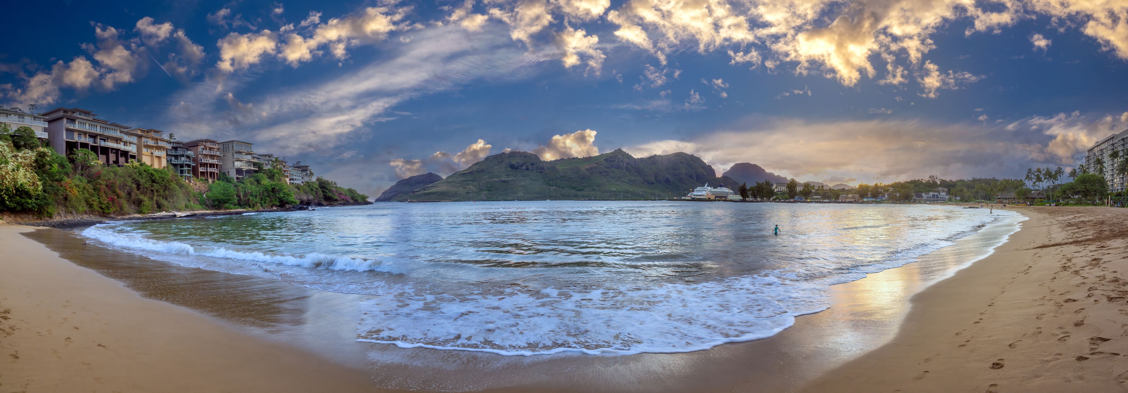 Uma praia com ondas, uma montanha e edifícios ao fundo.